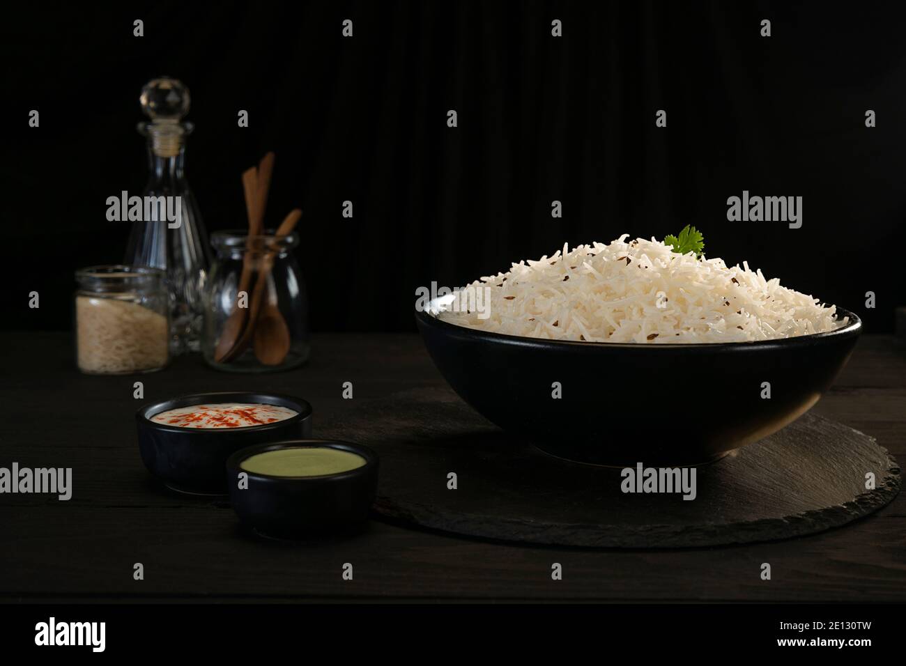 Steamed rice with Cumin in a black bowl with green chutney and curd ...