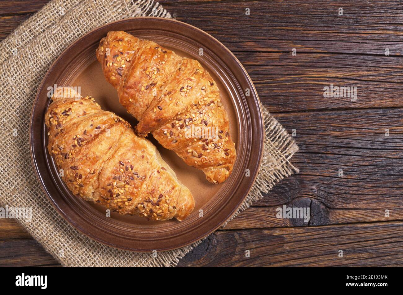 Two croissants with sesame seeds in plate on dark wooden table, top ...