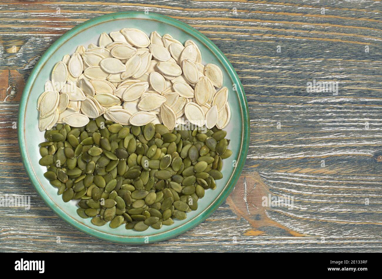 Pumpkin seeds peeled and in the shell in plate on old wooden background ...