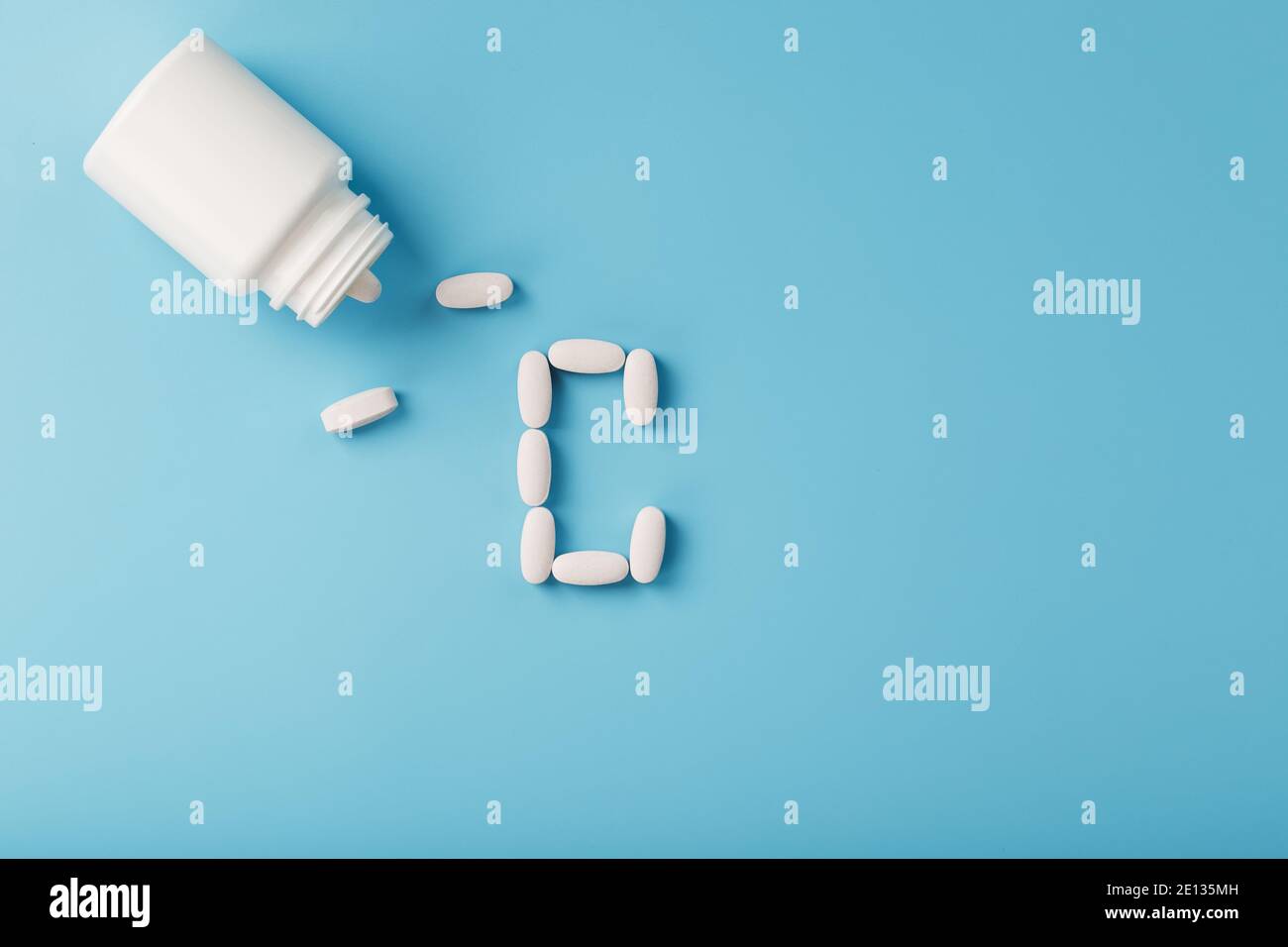 The letter of vitamin C in capsules pour out from the jar on a blue ...