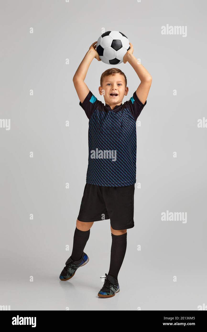 little boy football player in uniform with ball over studio background ...