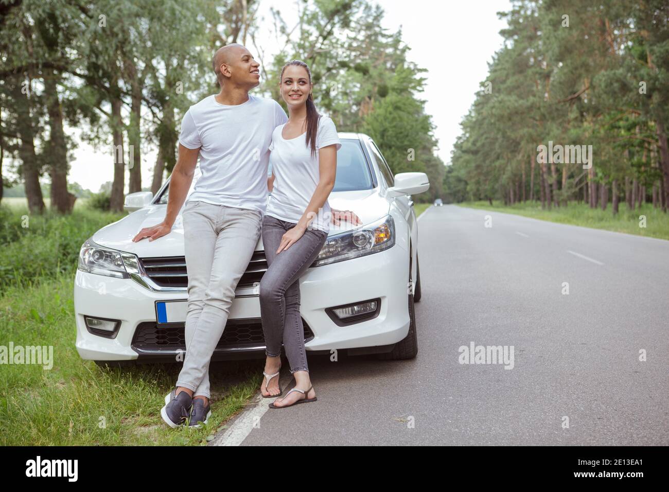 Happy young mixed race couple hugging near their car on the road ...