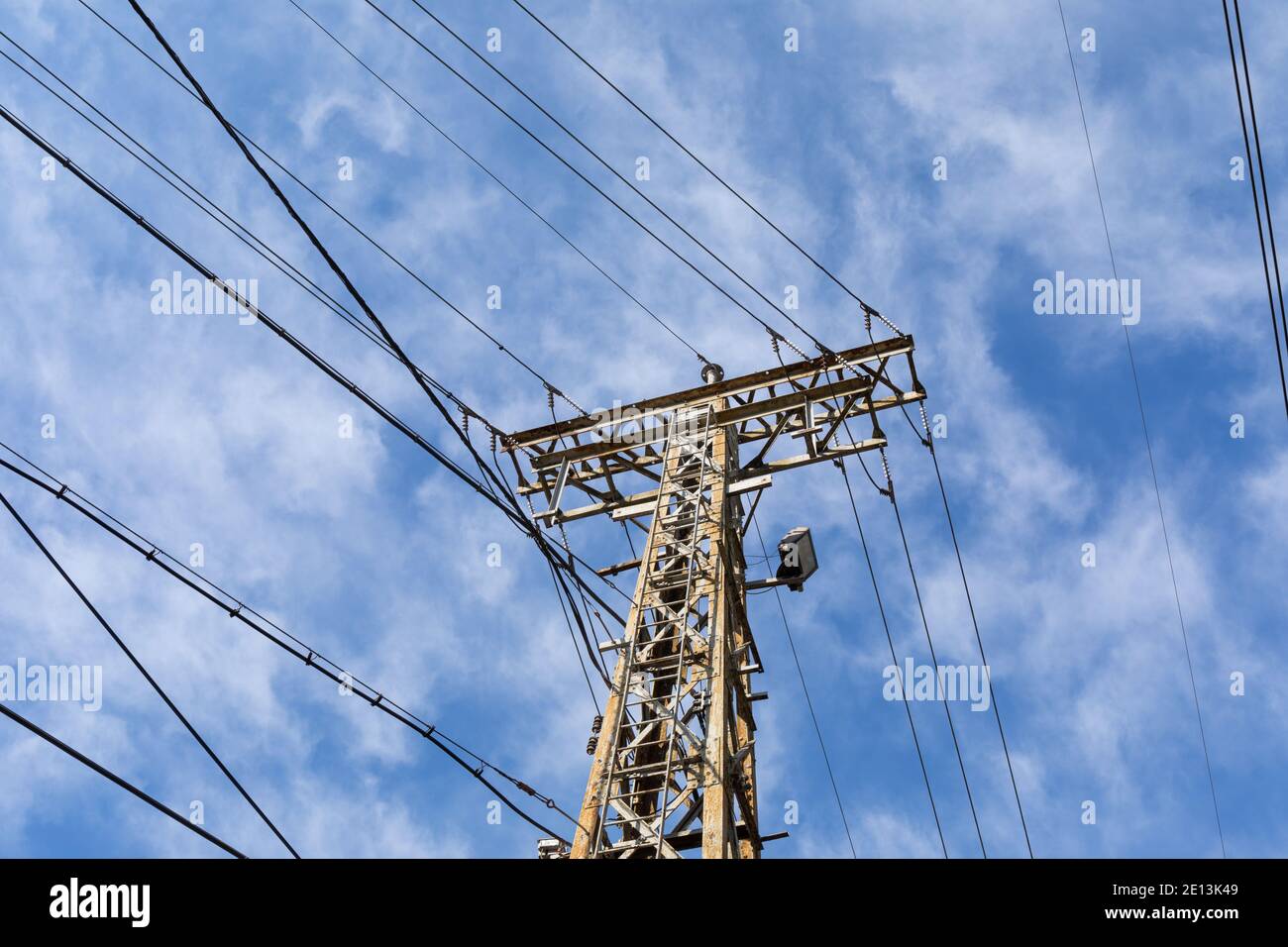 View looking up at a tall metal power tower and cables, deep blue sky ...