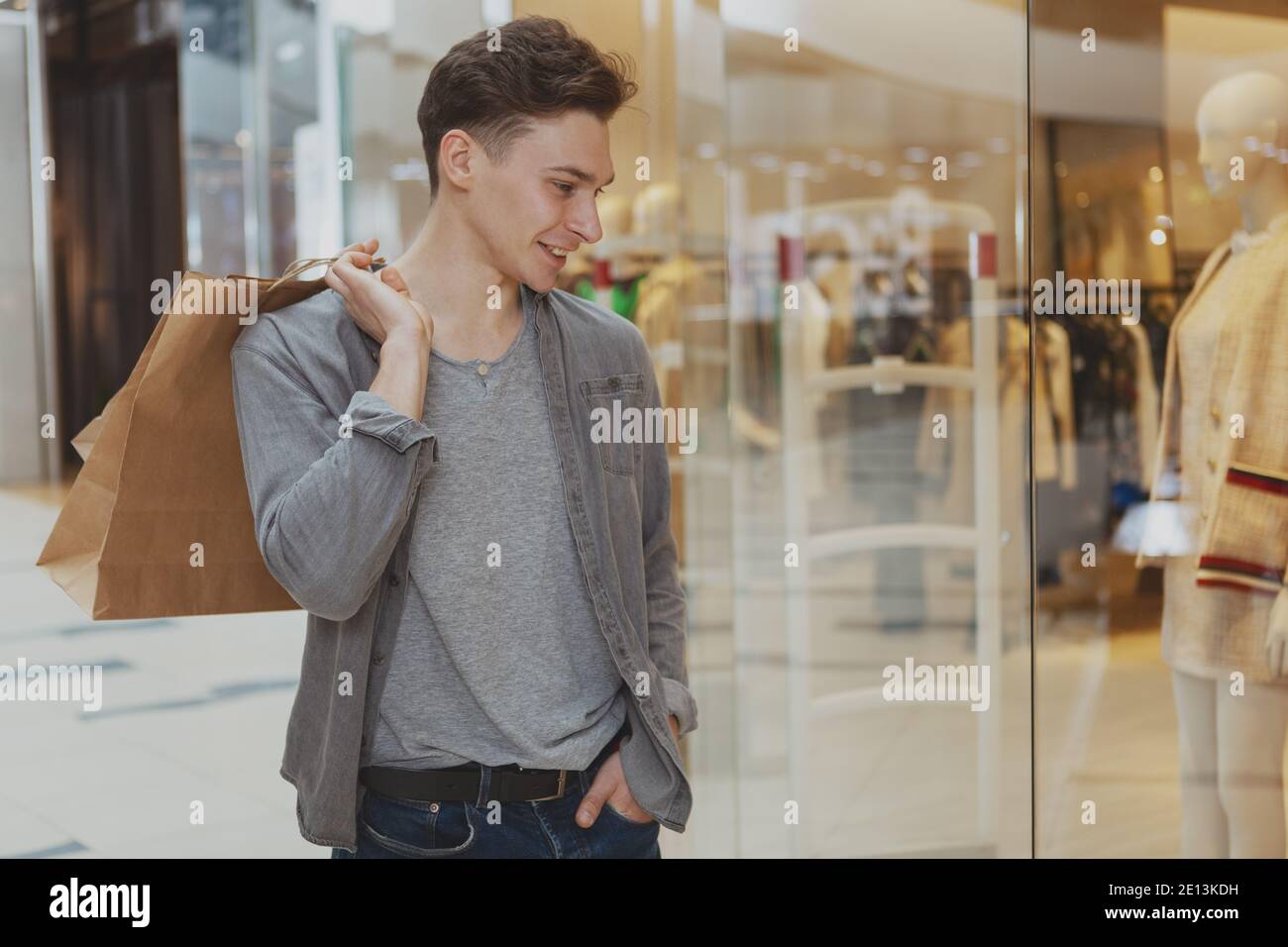 Attractive young man smiling, looking at the store showcase, walking at ...