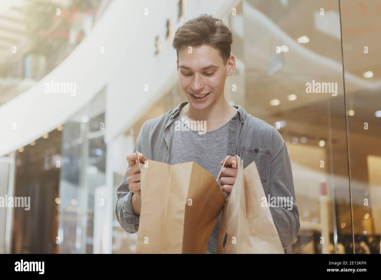 Charming young man smiling, looking inside his shopping bag, enjoying ...
