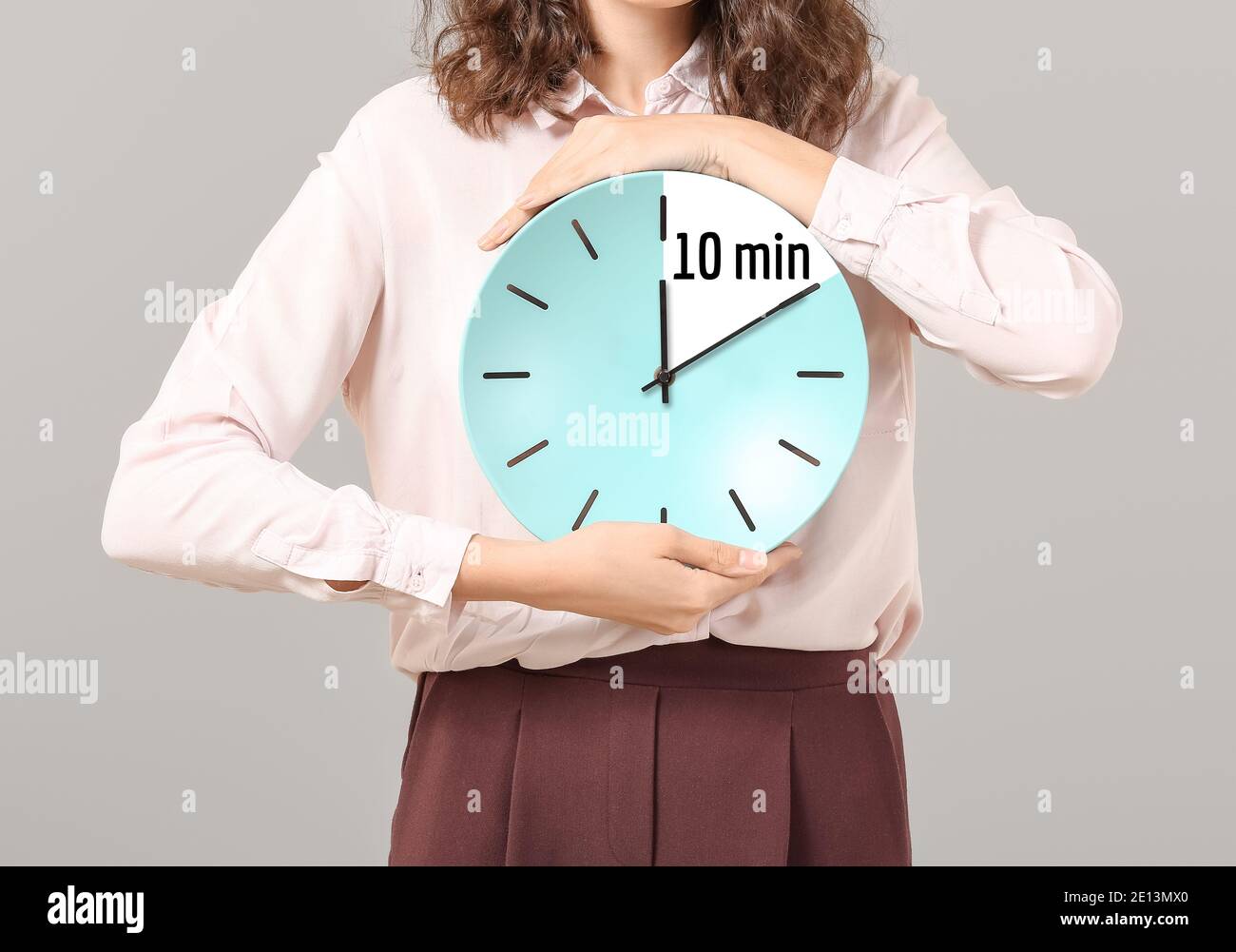 Businesswoman holding clock with timer for 10 minutes on grey ...