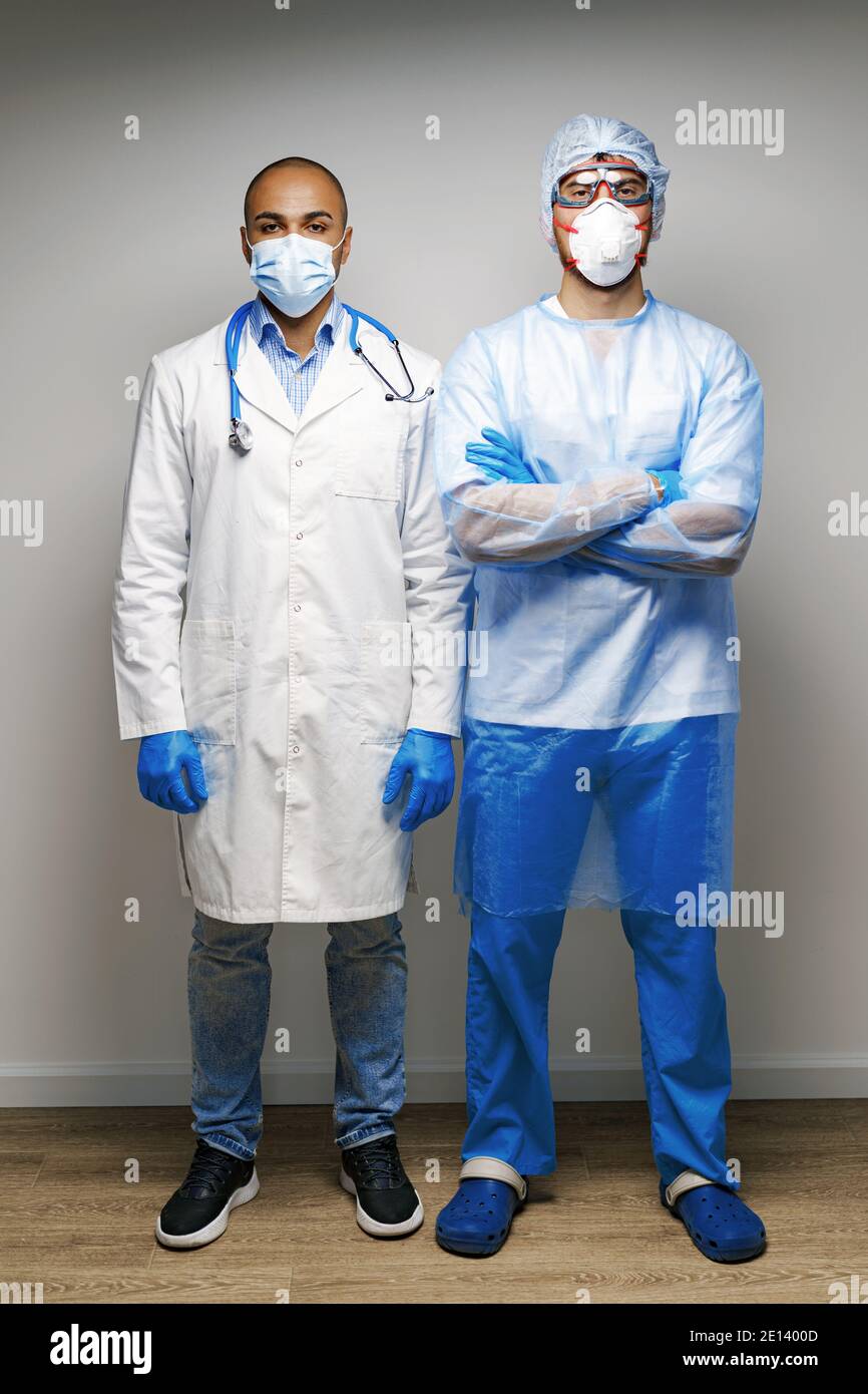 Male doctors in medical uniform wearing masks standing against grey ...