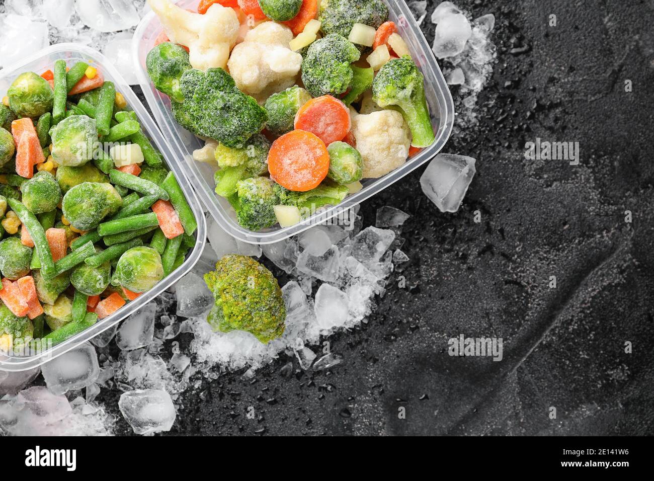 Plastic containers with frozen vegetables and ice on dark background ...