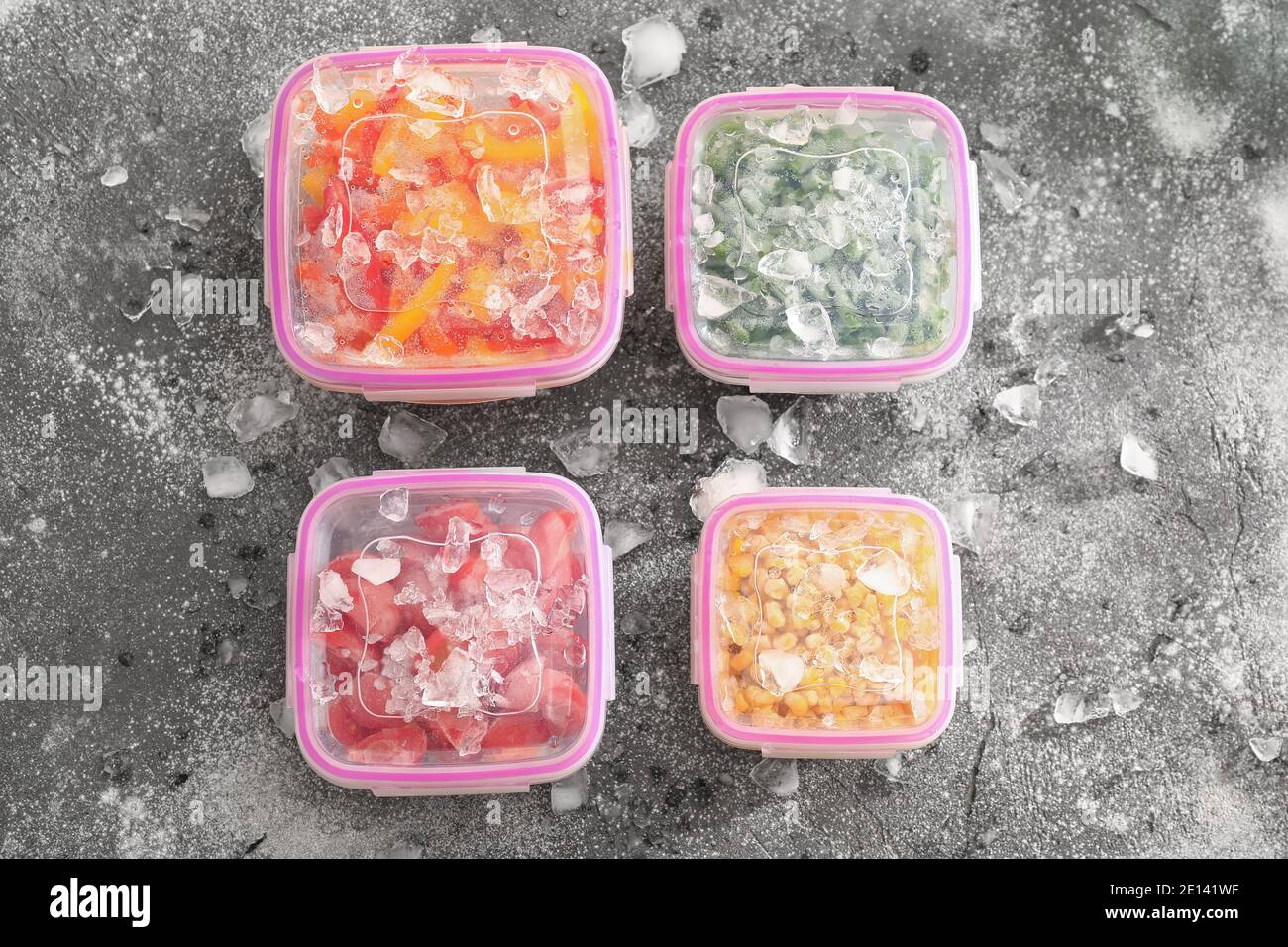 Plastic containers with frozen vegetables and ice on dark background ...