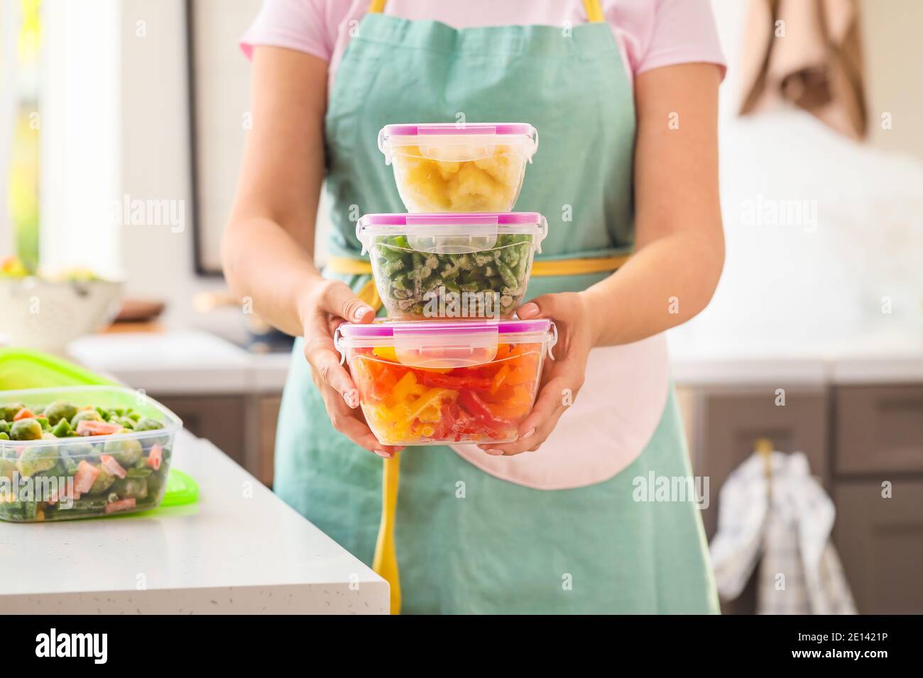 Woman holding plastic containers with frozen vegetables in kitchen ...