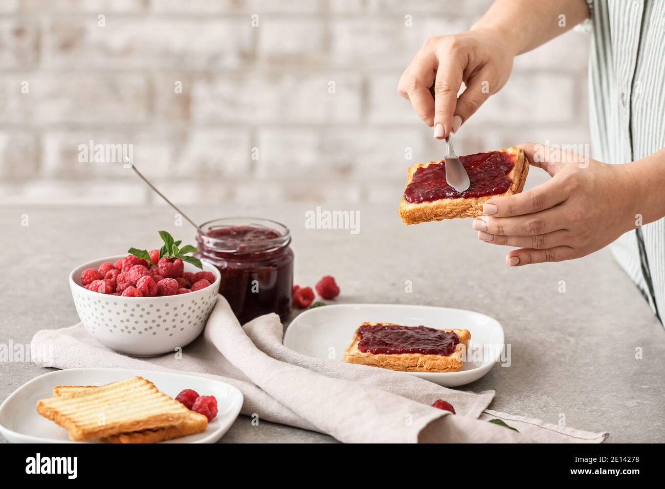 Woman spreading sweet raspberry jam on toast in kitchen Stock Photo - Alamy