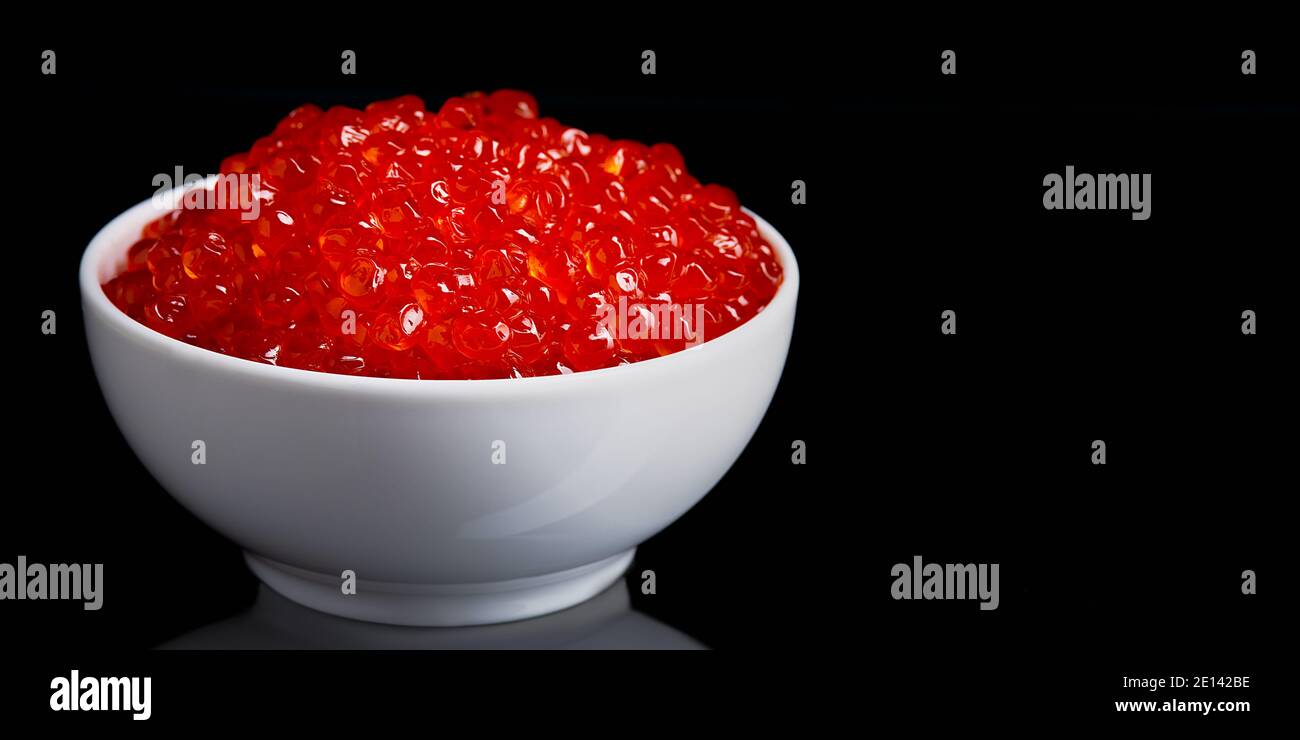 Red caviar in a white cup on a black background with a reflection ...