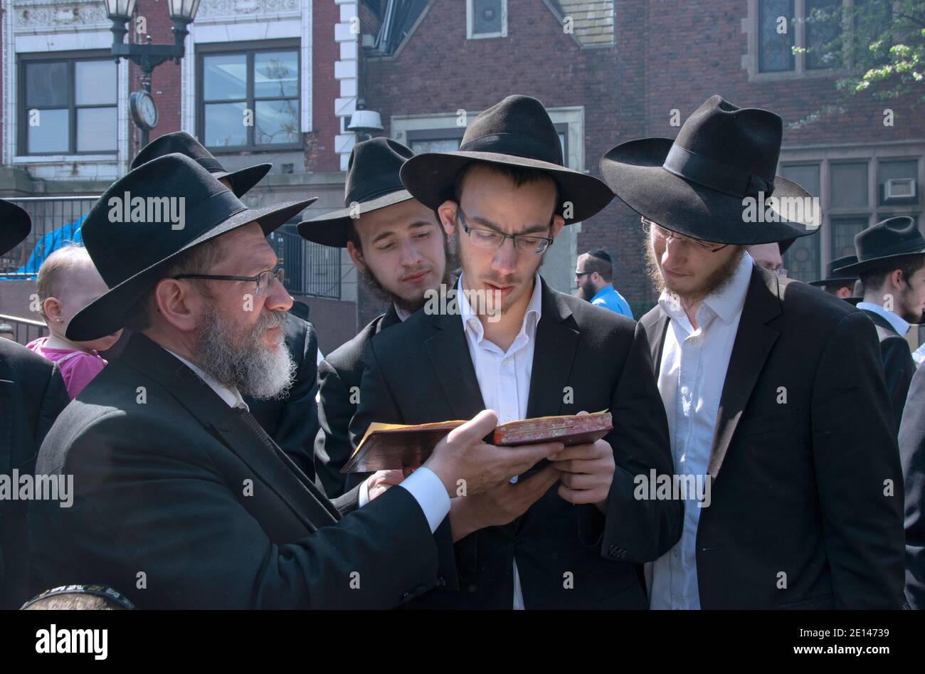A group of Jewish men of varying ages share a prayer book at the annual ...