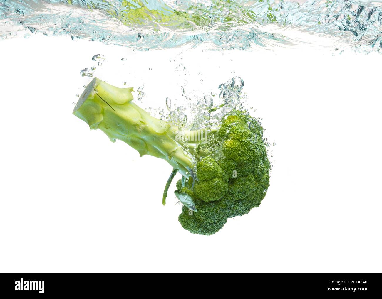 Green broccoli falling in water with splash on white with air bubbles ...