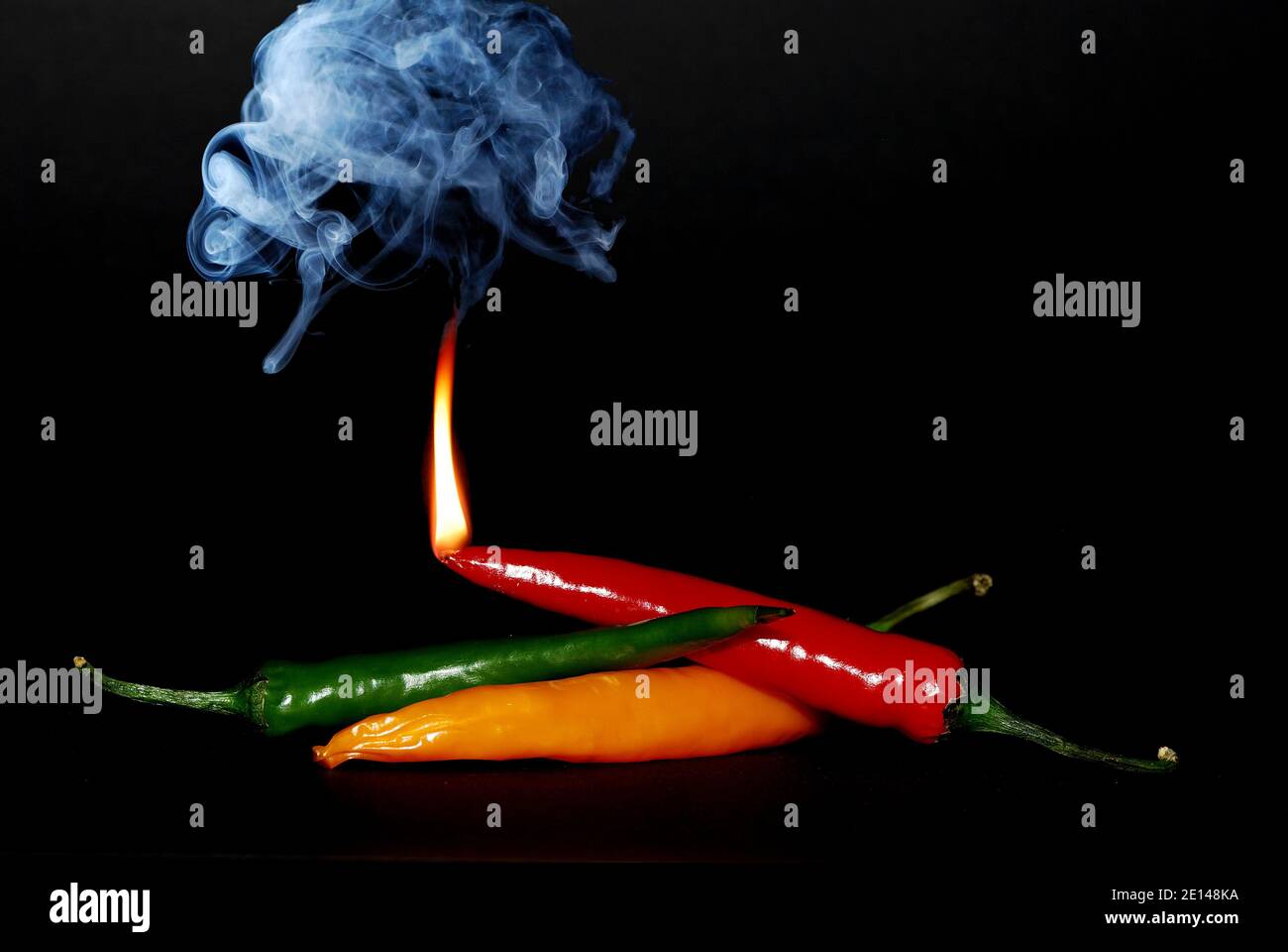 three different colored chilli pepper with flame and smoke on black ...