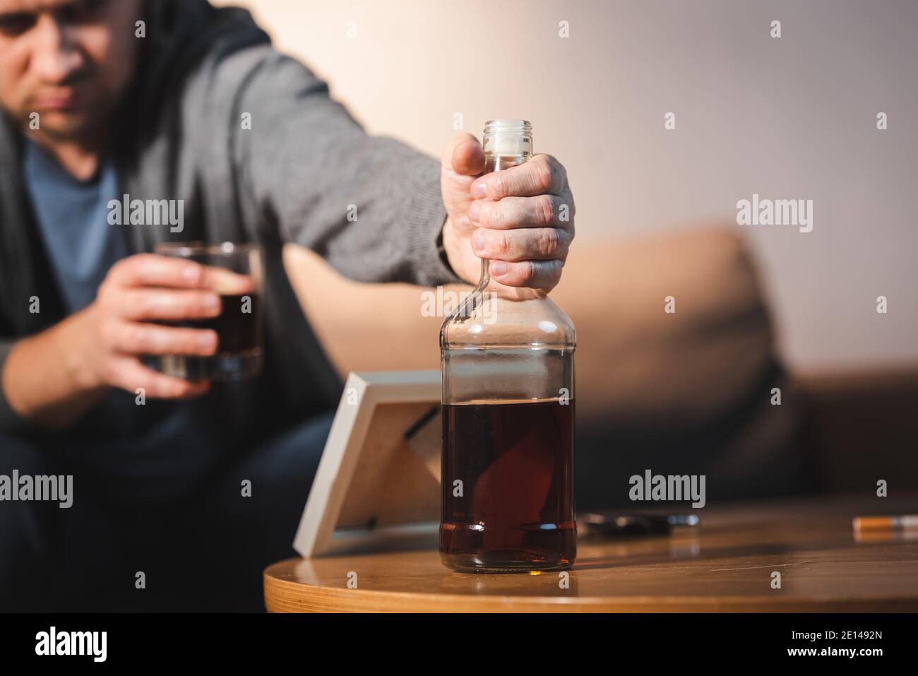 drunk man taking bottle of whiskey near photo frame on table, blurred ...