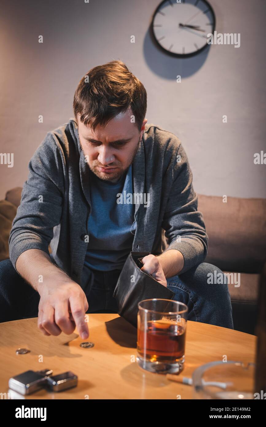 drunk man holding empty wallet near coins and glass of whiskey on ...