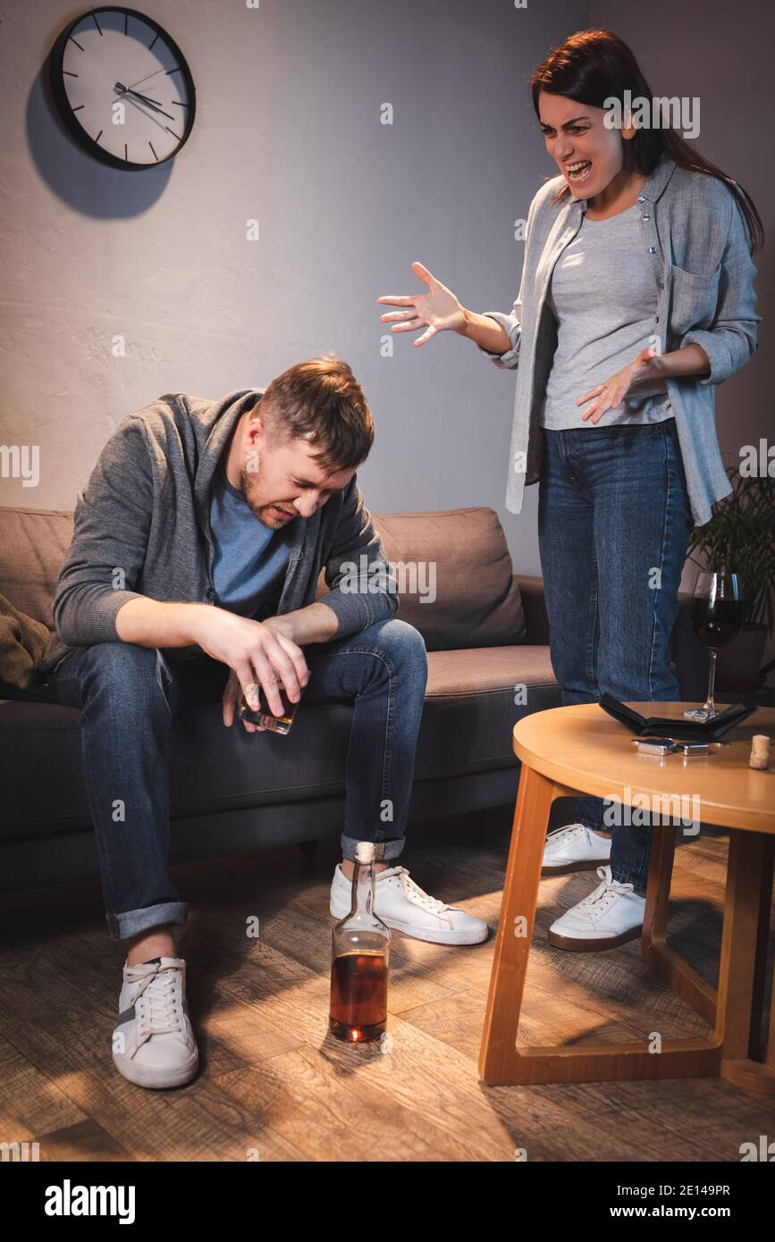 aggressive wife shouting at drunk husband sitting on sofa with bowed ...