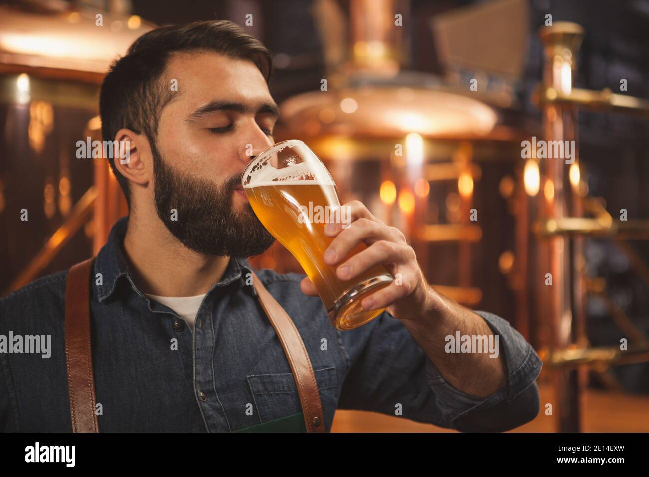 Bearded male brewer sipping delicious ber from a glass, working at his ...