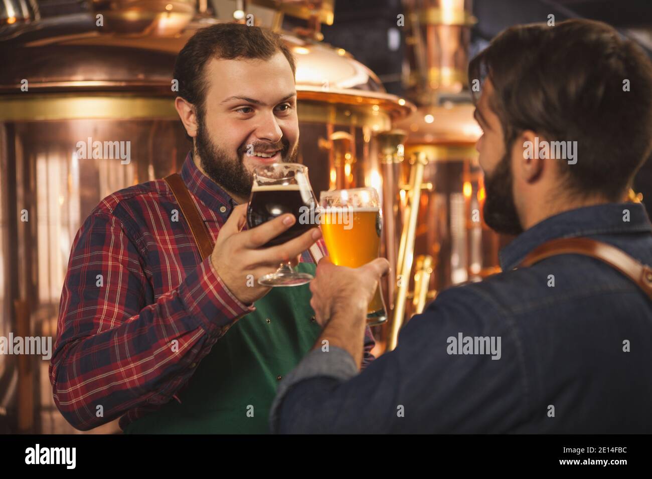 Bearded cheerful brewer talking to his assistant, working at the beer ...