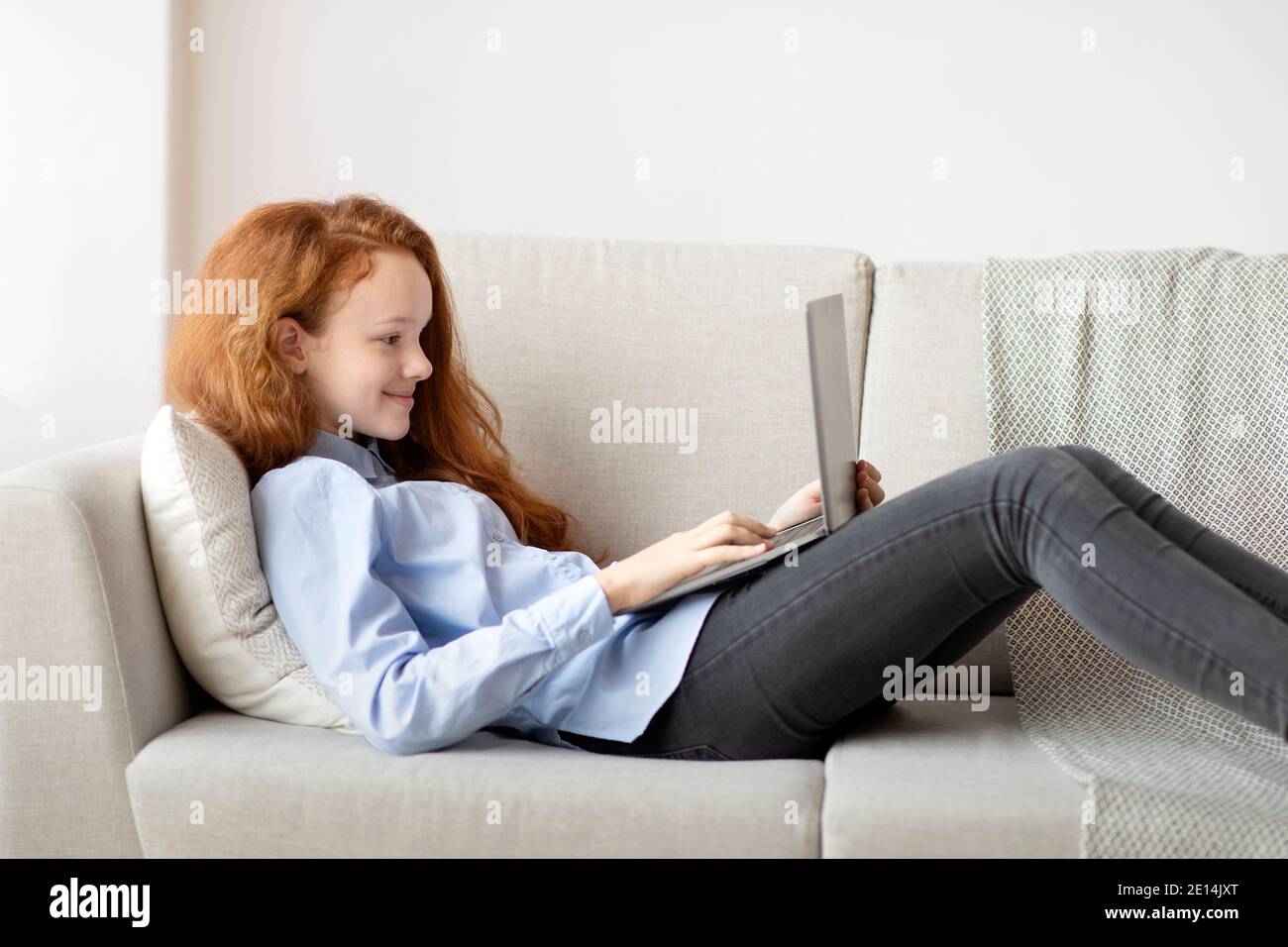 Girl lying on couch and using her laptop computer Stock Photo - Alamy