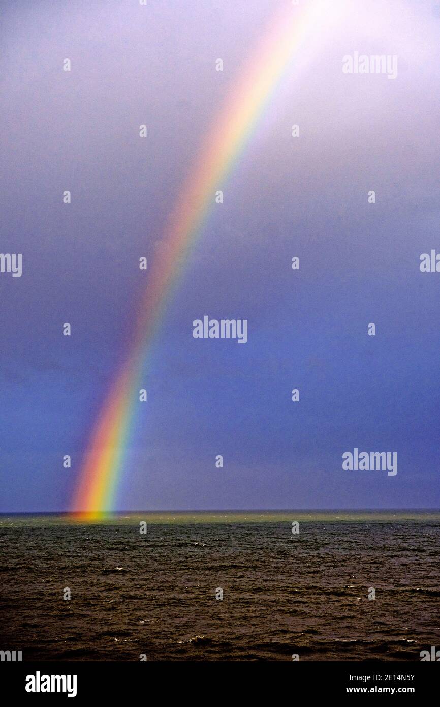 Rainbow arcing left to right entering the sea during showers Stock ...