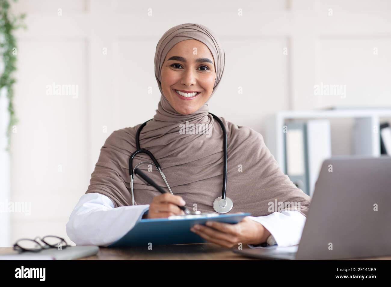 Beautiful muslim woman doctor writing in medical chart Stock Photo - Alamy