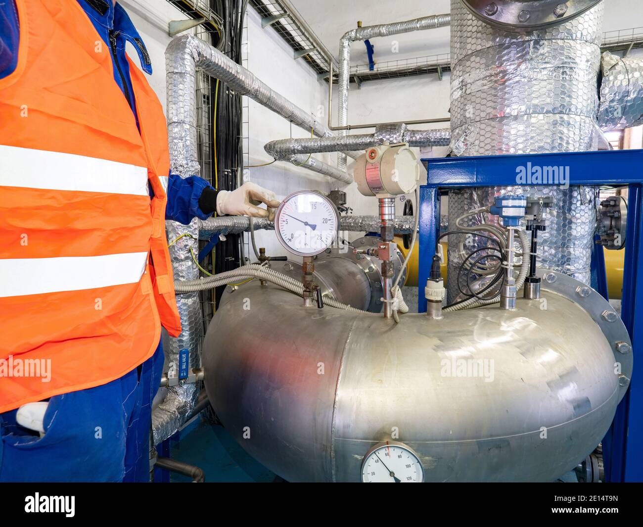 Worker stands by a chrome pipe with pressure and temperature control ...