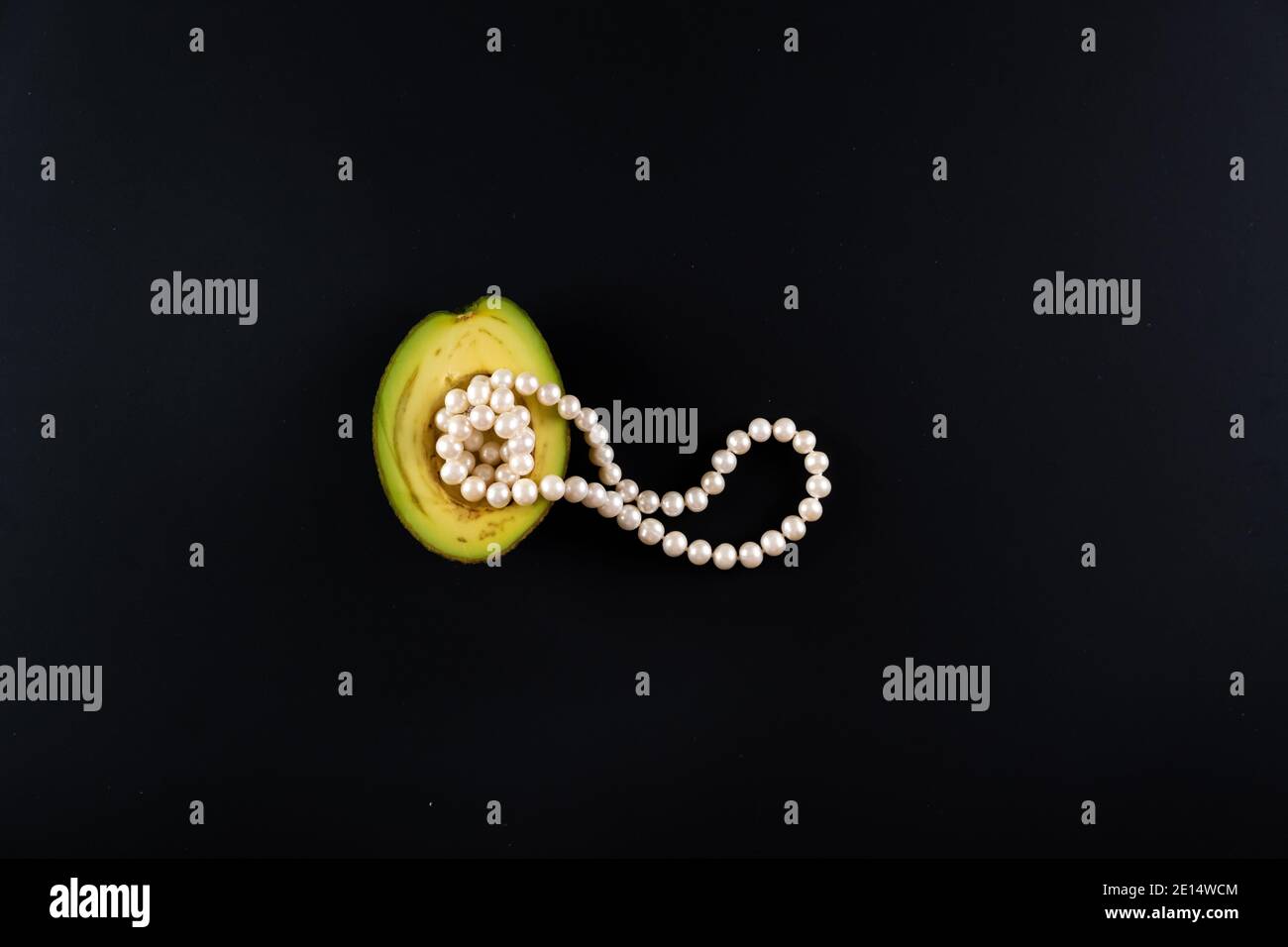 half an avocado with pearls on a black background. surrealism ...