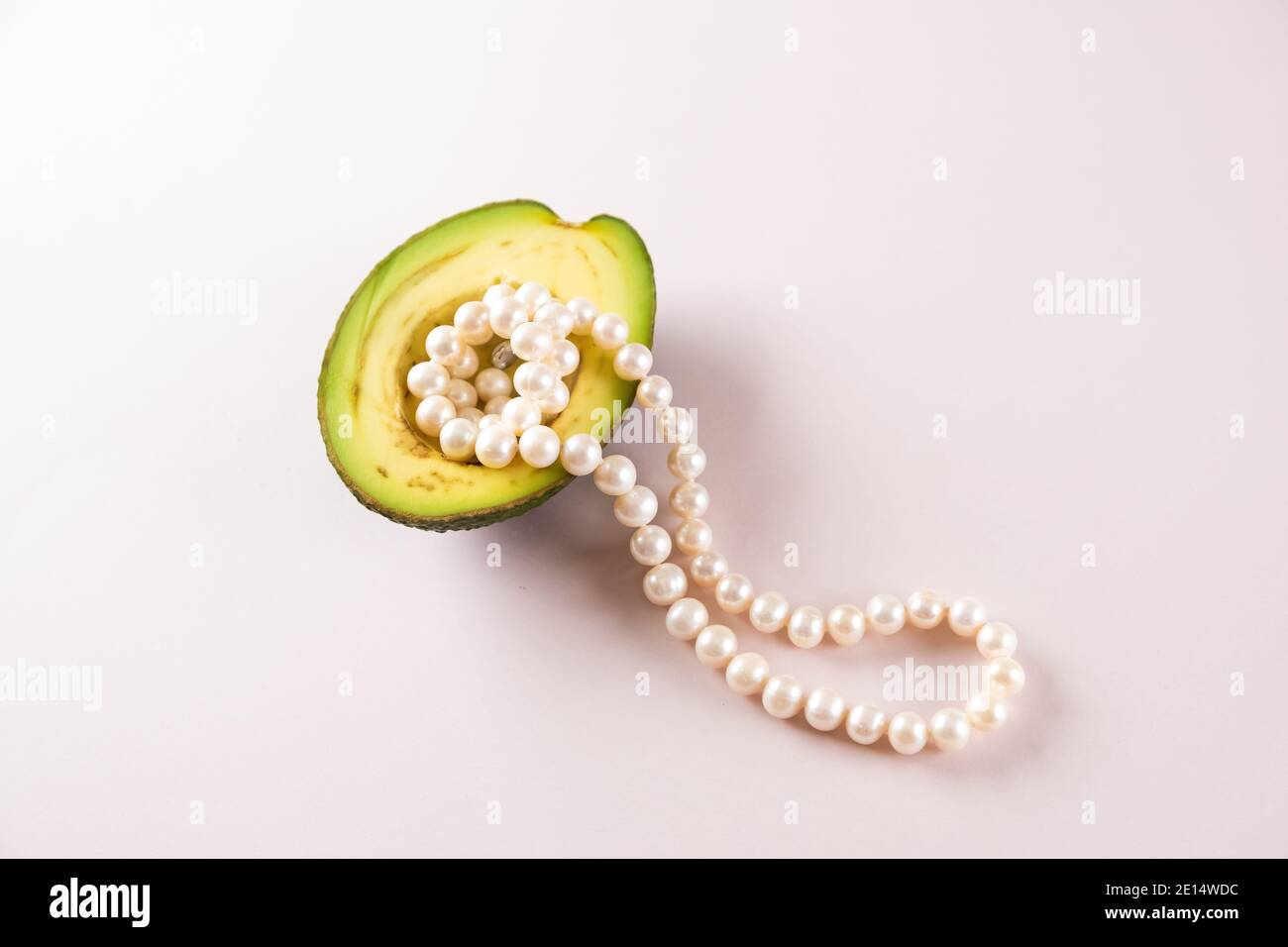 half an avocado with pearls on a light pink background. surrealism ...