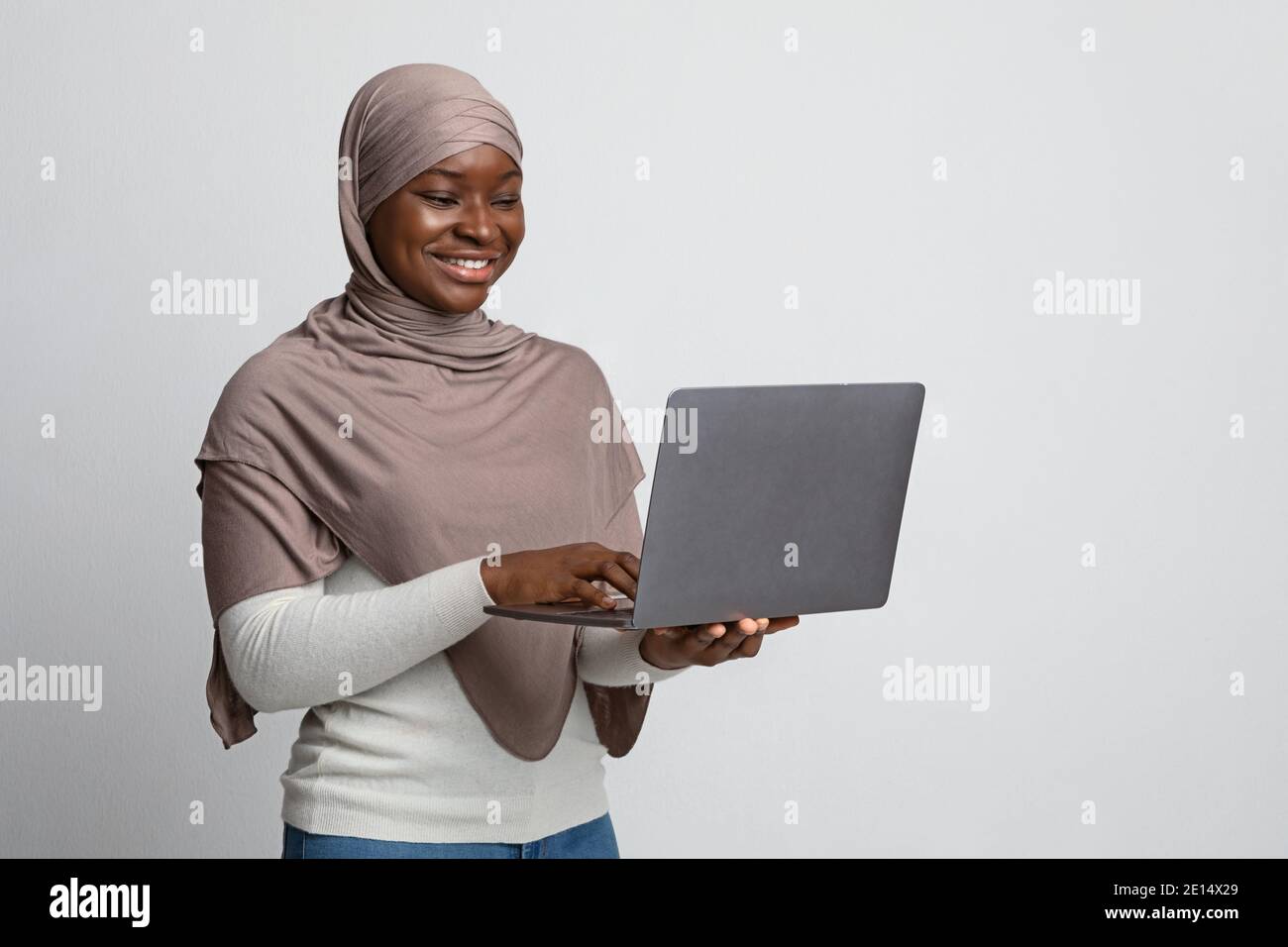 Smiling Black Muslim Lady In Hijab Holding Laptop, Typing On Keyboard ...