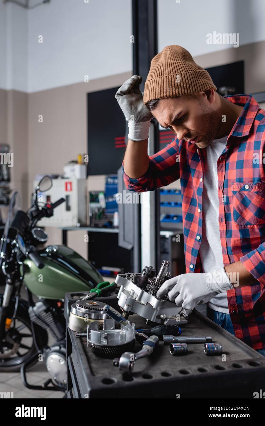 young mechanic touching head while checking disassembled motorcycle ...