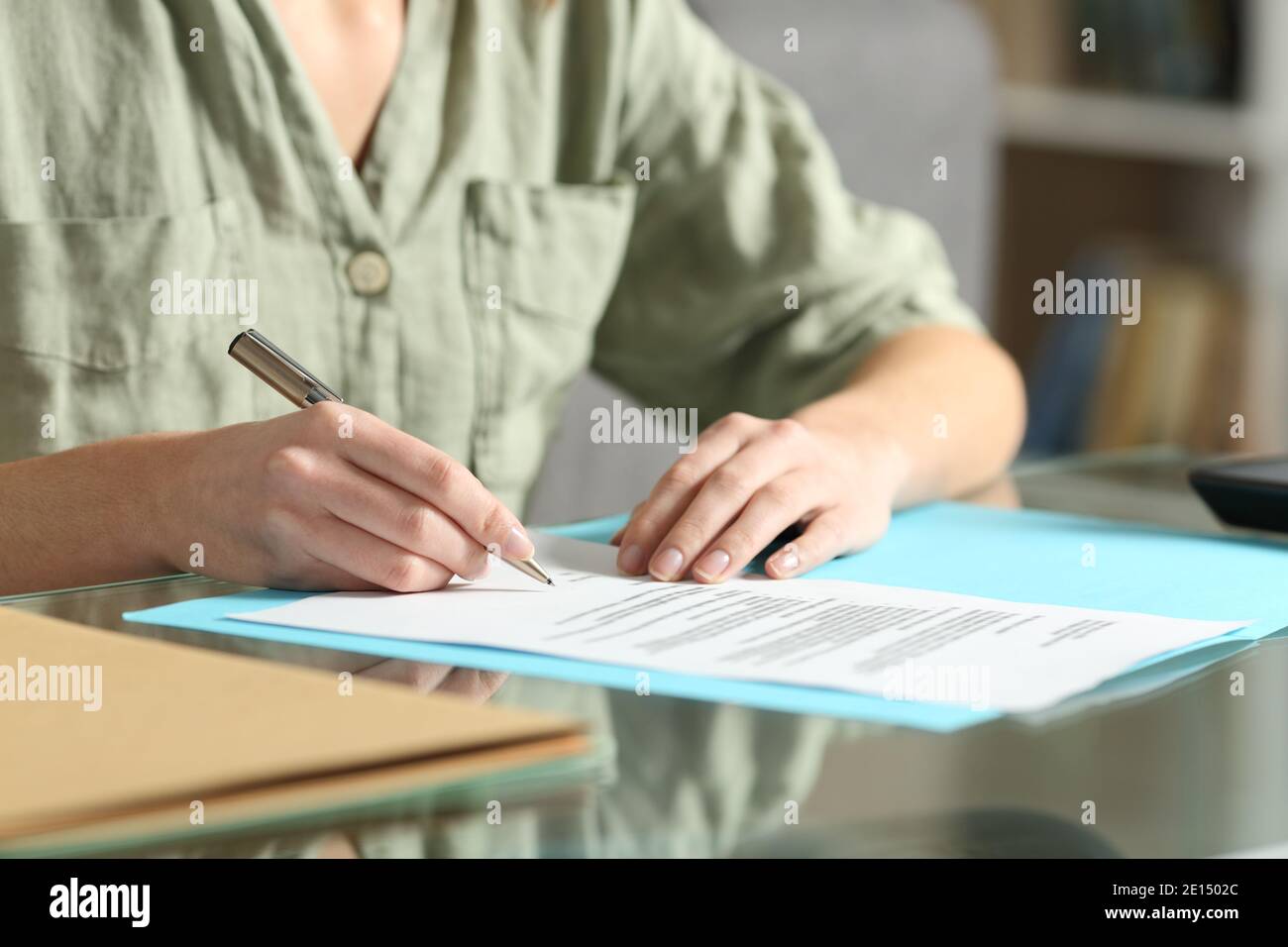 Close up of a woman hands signing contract on a glass table at home ...