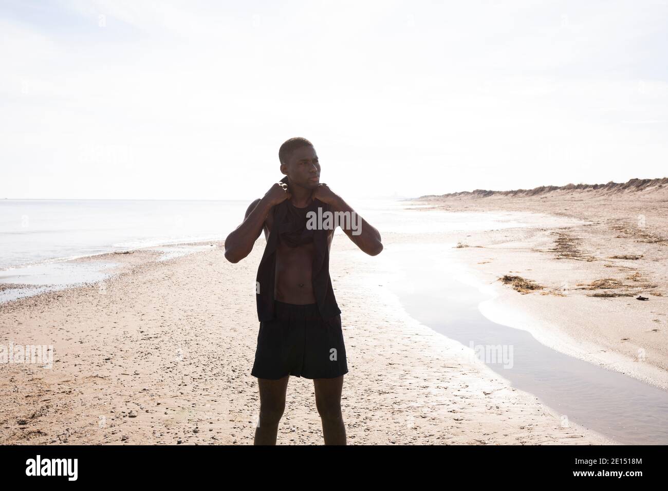 Healthy young athletic man wearing sport clothes at the beach with back ...
