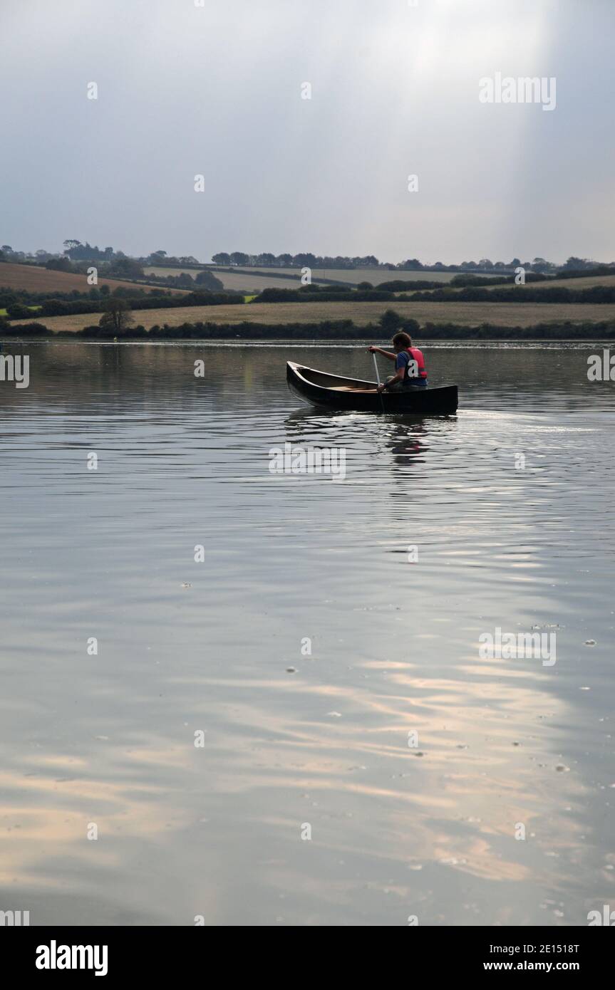 Young lady paddling a Canadian canoe in calm water on a Cornish estuary ...