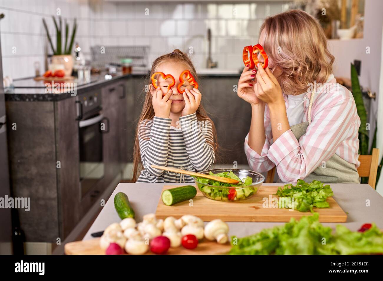 mom and daughter have fun while cooking in the kitchen, adorable woman ...
