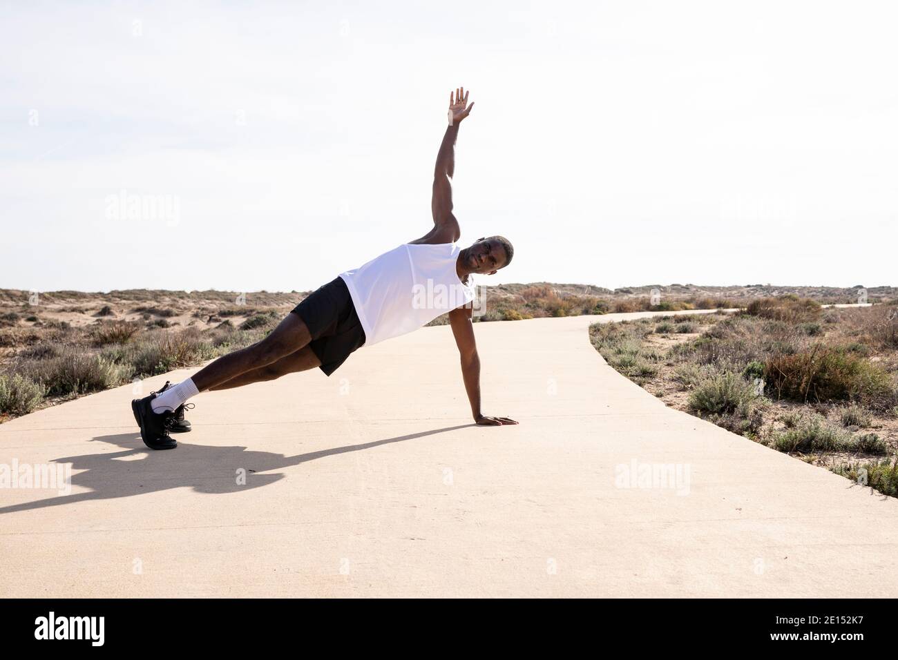 Young black runner in profile doing push-ups and lifting one arm and ...