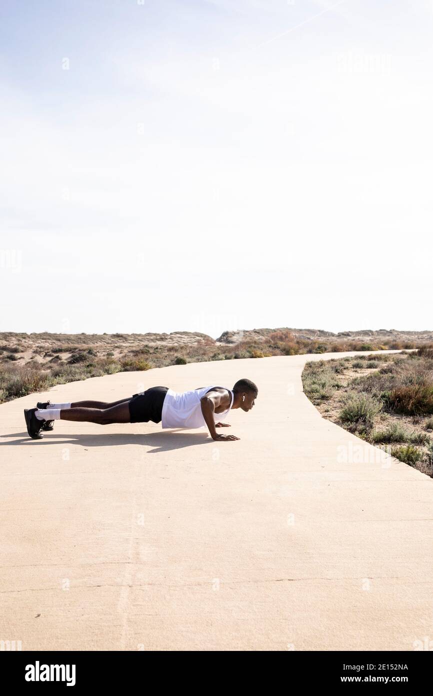 Vertical shot of young black runner in profile doing push-ups and ...