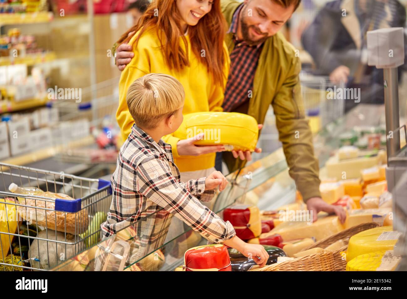 family with son choosing cheese in food store, looking at showcase with ...