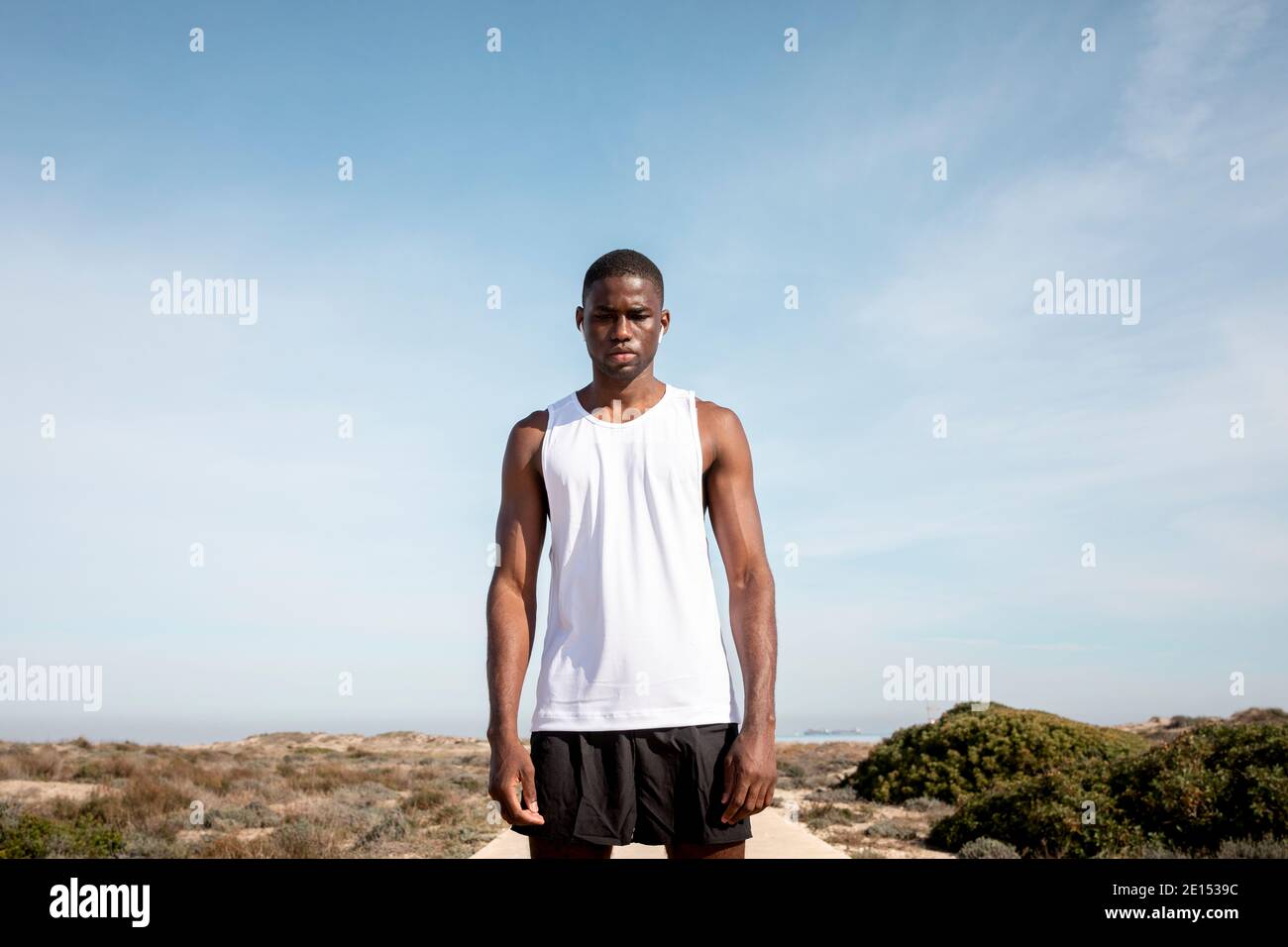 Medium shot of young black runner standing and looking at camera after ...
