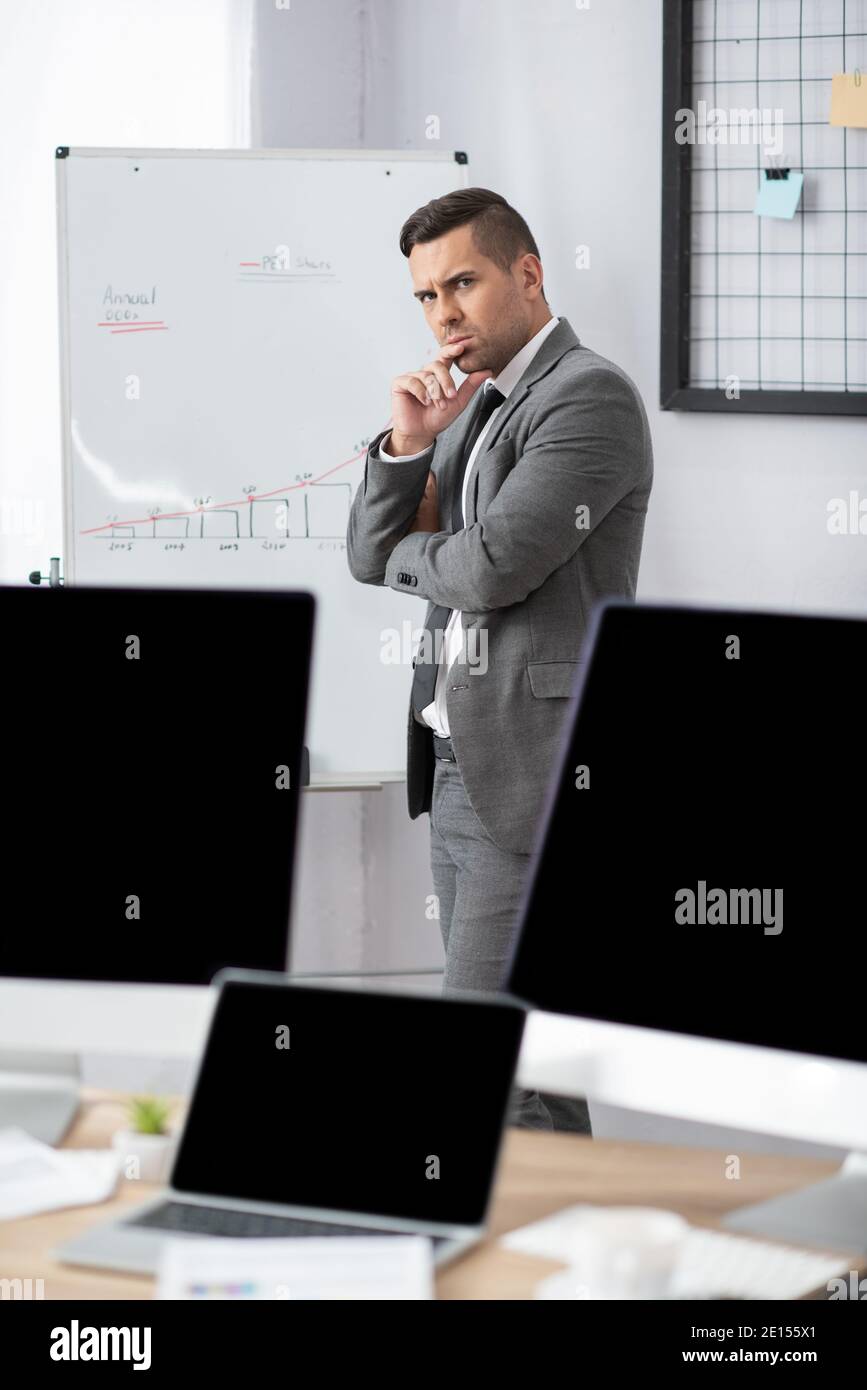 thoughtful trader standing at flipchart with graphs near monitors with ...