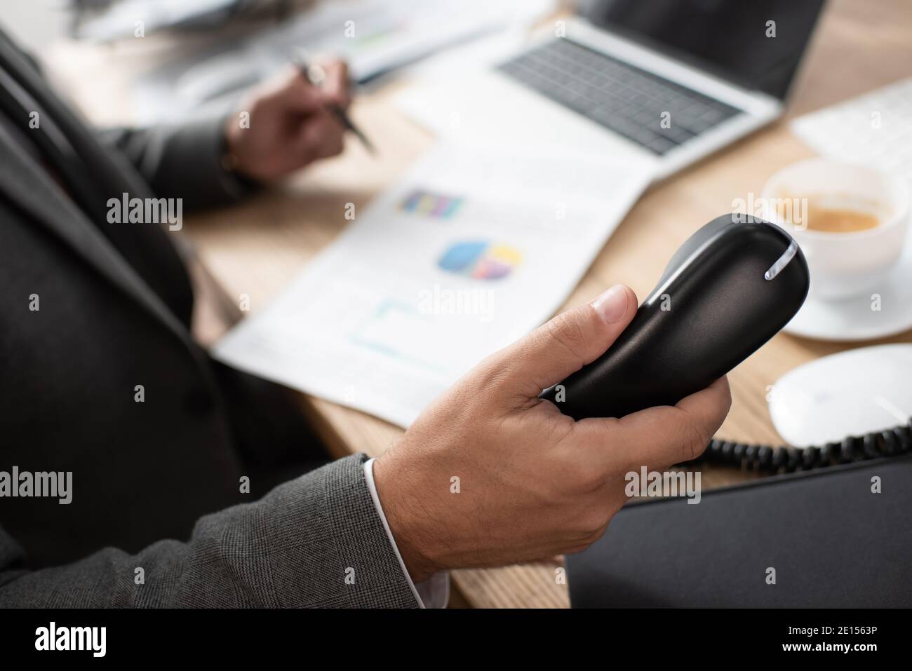 partial view of trader holding handset of telephone, blurred background ...