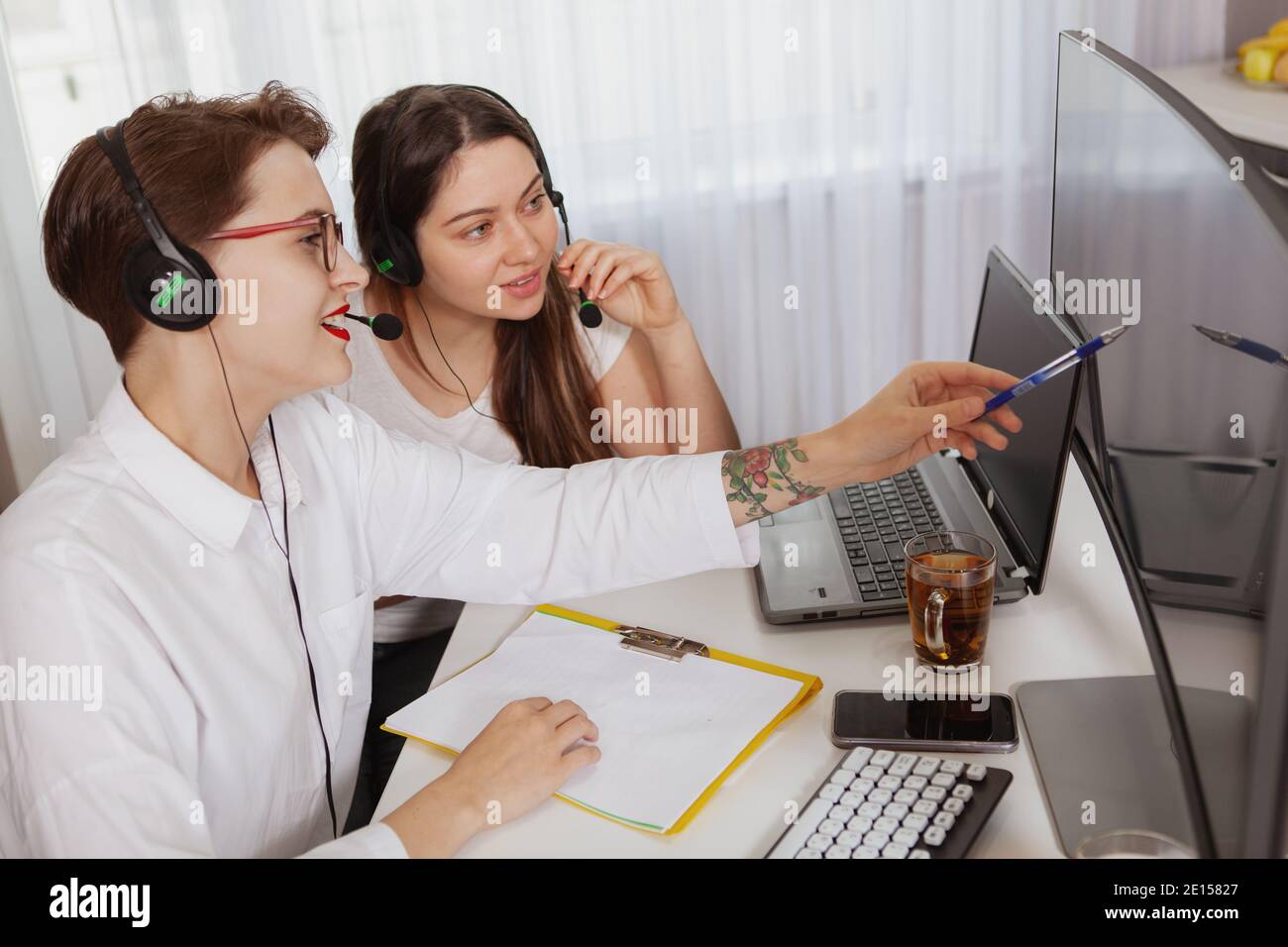 Two female call center operators talking at work. Helpdesk employees ...