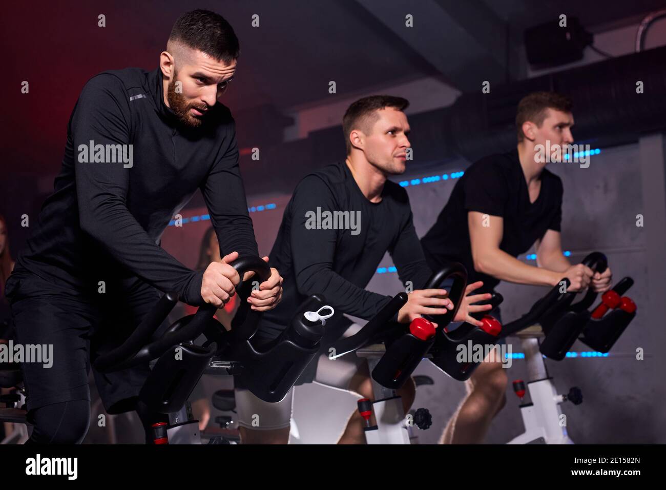 three fitness men riding exercise bikes in gym, they lead healthy ...