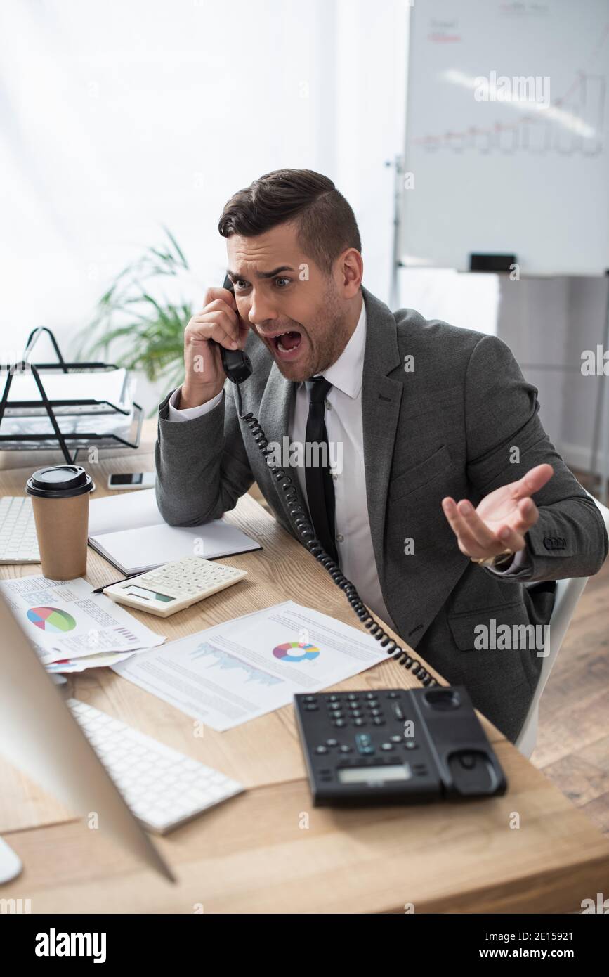 angry trader screaming while talking on landline phone near papers with ...
