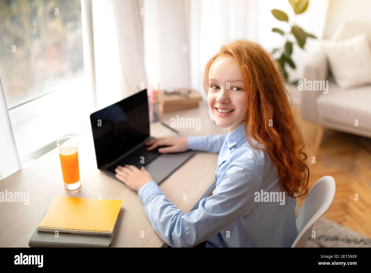 Girl using laptop for elearning, looking back at camera Stock Photo - Alamy
