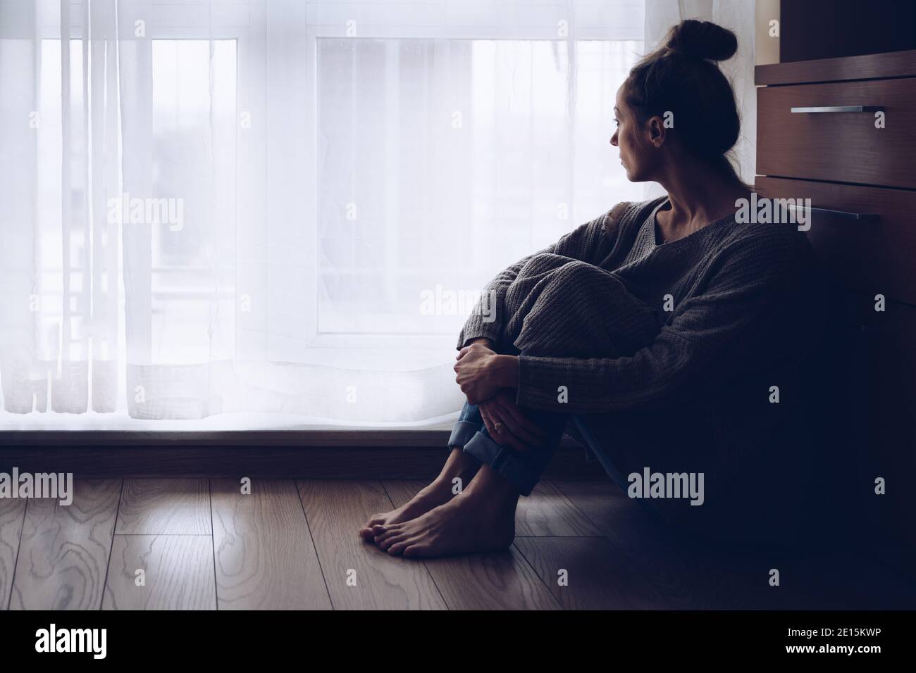 Sad woman sitting on the floor in her living room looking out the ...