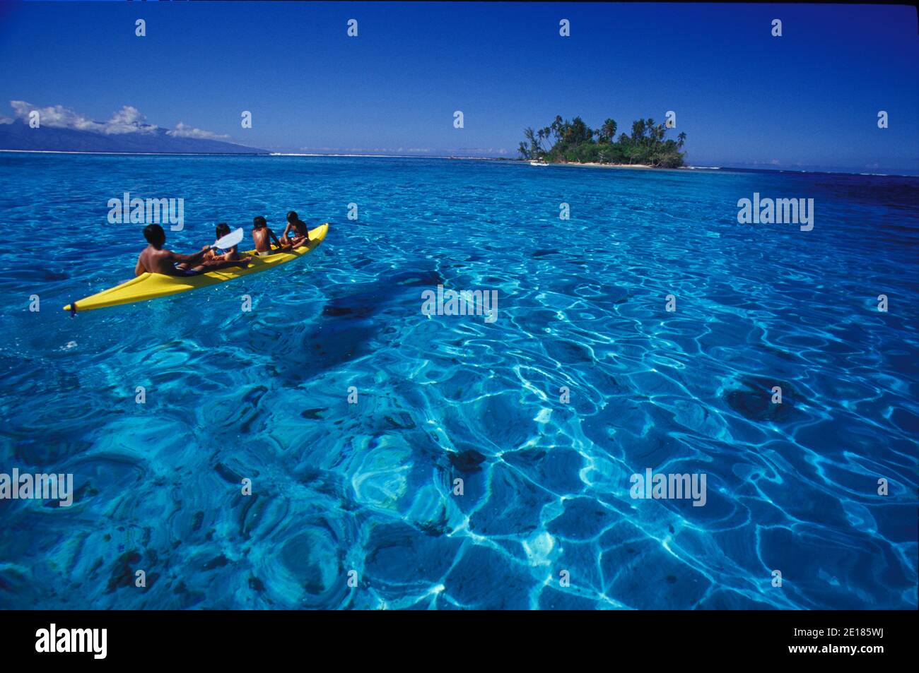 Parent and children paddling a kayak to a 'motu' islet in the clear ...