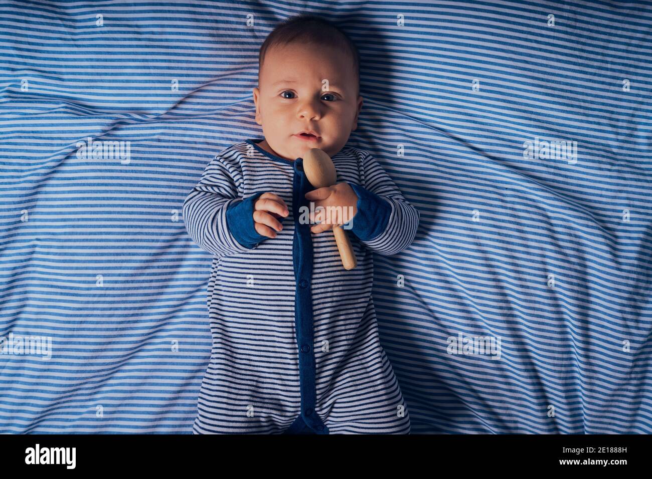 A little baby is lying on a bed with a wooden rattle Stock Photo - Alamy