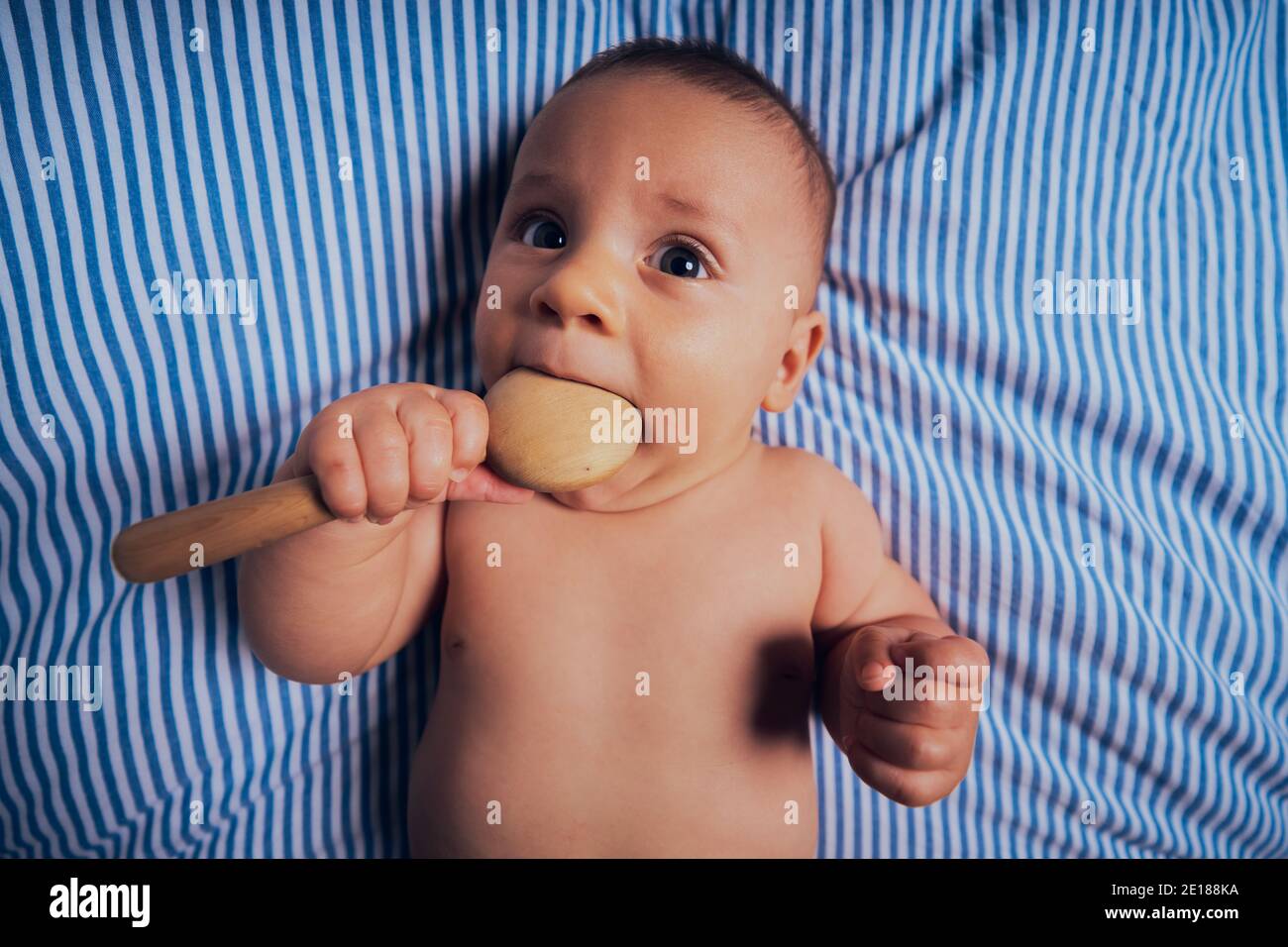 A little baby is lying on a bed with a wooden rattle Stock Photo - Alamy